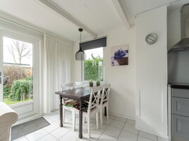 Uma sala de jantar com uma mesa, cadeiras, um lustre, um relógio e vista para o verde lá fora.