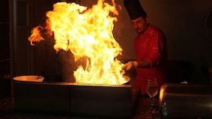 Um chef fazendo um flambé com uma chama grande em uma cozinha.