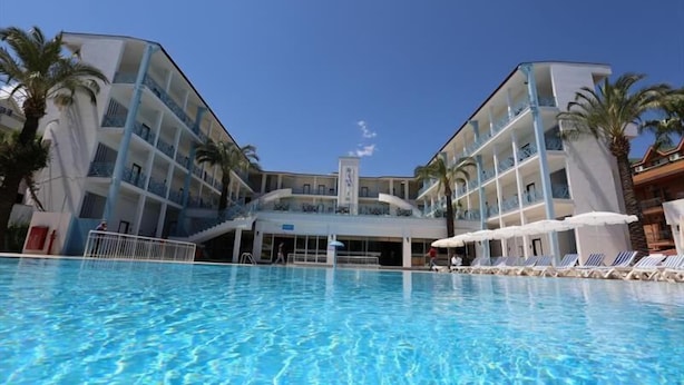 Um hotel com piscina, várias varandas e palmeiras.