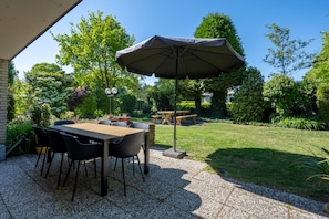 Um pátio externo com mesa, cadeiras, mesa de piquenique e guarda-sol.