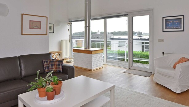 Sala de estar moderna com lareira, sofá, mesa de centro com plantas e vista através de grandes portas de vidro.