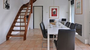 Uma sala de jantar com uma mesa branca, cadeiras pretas, uma escada de madeira e uma porta.