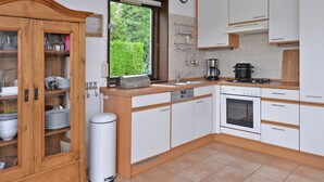 Uma cozinha moderna com armários brancos, um aparador de madeira com portas de vidro, uma janela com vista para o verde e um relógio na parede.