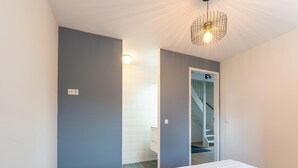Quarto com cama, luminária e porta que dá para uma escada.