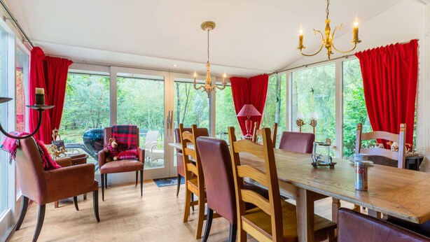 Uma sala de jantar com uma mesa e cadeiras de madeira, cortinas vermelhas e um candelabro.