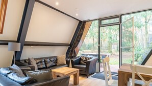 Uma sala de estar moderna com sofá, mesa de centro e vista para um jardim através de grandes janelas.