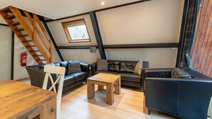 Uma sala de estar estilo loft com escada de madeira, sofás de couro, mesa de centro de madeira e uma pequena janela.