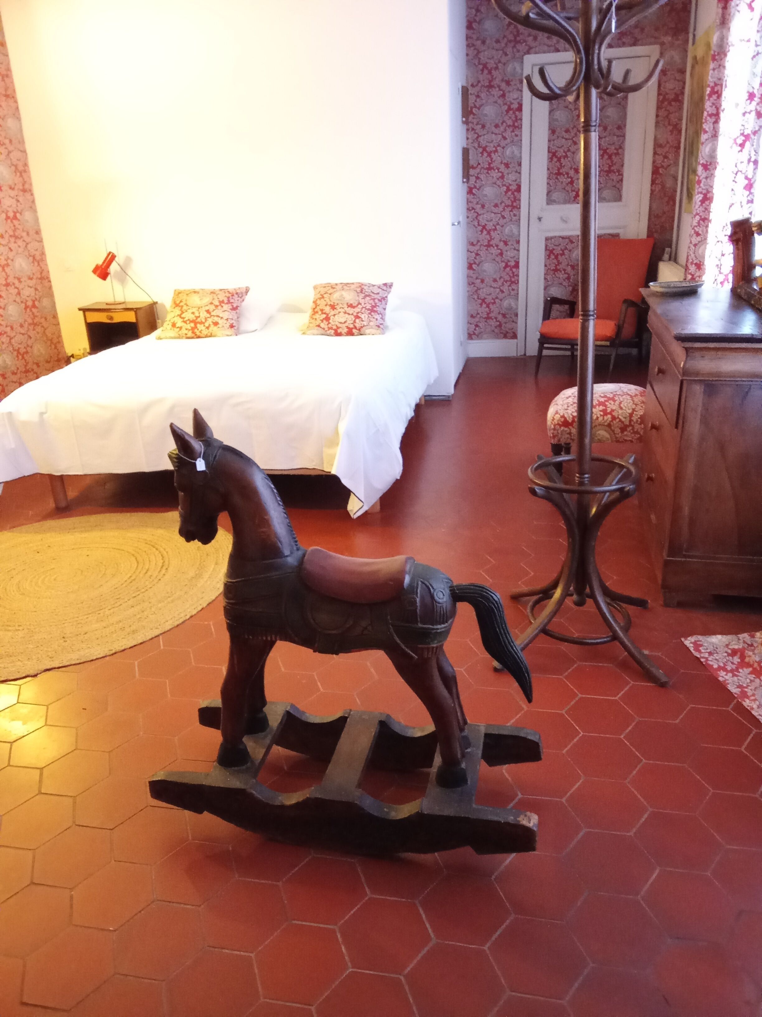 Um quarto com cama, um balanço de madeira, uma cadeira, uma escrivaninha e um cabideiro.