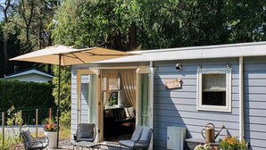 Uma casa com um pátio, mobiliário de exterior, um espaço de estar coberto e vasos com plantas.