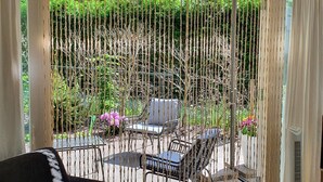 Quarto com vista para um jardim, visível através de uma divisória de bambu. Há áreas de estar ao ar livre e uma mesa.