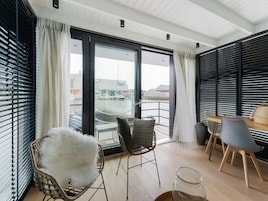 Quarto moderno com uma grande porta de vidro deslizante que dá para uma varanda, cadeiras de vime, uma mesa pequena e um pote de vidro no chão.