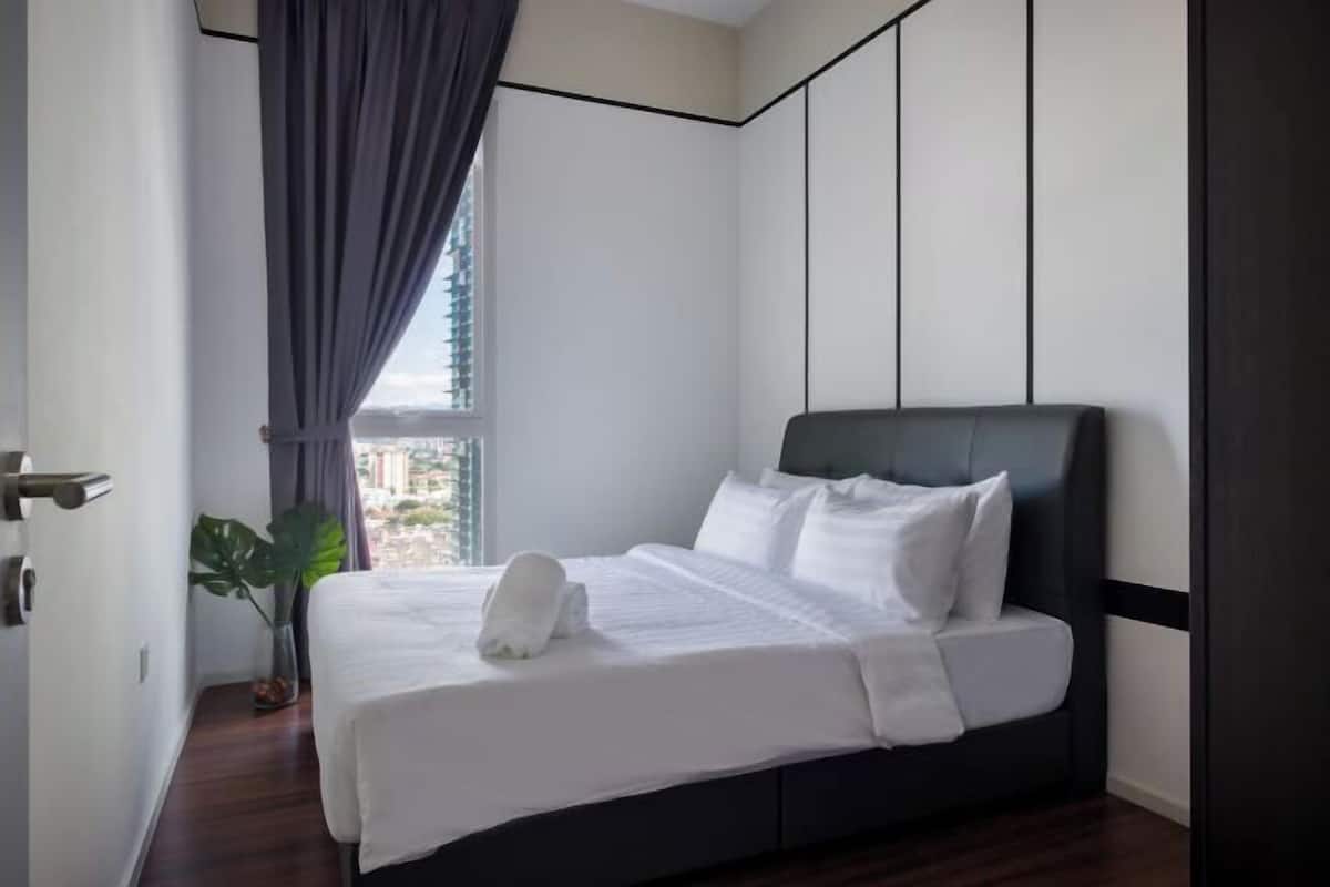 Quarto de hotel moderno com uma cama grande, uma janela com cortinas e vista para a cidade.
