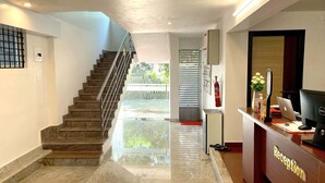Uma área de recepção com piso de mármore, uma escada e um balcão com computador e telefone.