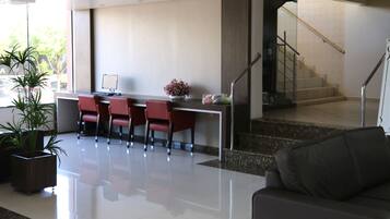 Um lobby moderno com uma mesa de recepção, cadeiras vermelhas, uma planta em vaso e uma escada.