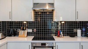 Uma cozinha moderna com armários brancos, painel de azulejos preto, coifa de aço inoxidável e forno embutido.