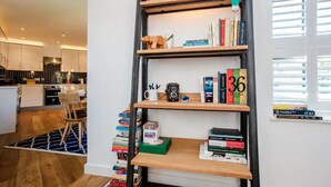 Uma cozinha moderna com armários brancos, uma mesa de jantar de madeira e uma estante repleta de livros e objetos decorativos.