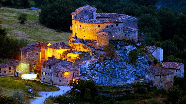 Um castelo medieval com vários edifícios, uma torre central e um fosso ao redor.