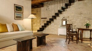 Uma sala de estar aconchegante com sofá, uma mesa de centro e uma mesa de jantar com cadeiras. Uma escada leva a um andar superior.