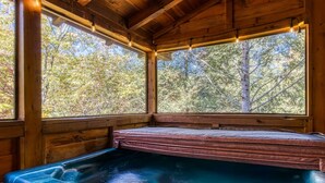 Uma cabana de madeira com banheira de hidromassagem, janelas amplas e vista para as árvores.