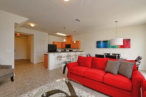 Uma sala de estar moderna com um sofá vermelho, uma mesa de centro de vidro e uma área de cozinha com armários de madeira e um micro-ondas.