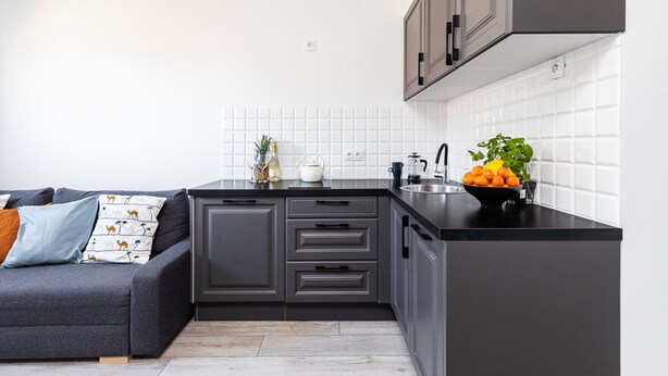 Cozinha moderna com armários cinza, bancada preta e painel de azulejos branco.