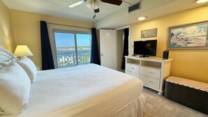 Quarto de hotel com uma cama grande, televisão, penteadeira e varanda com vista para o mar.