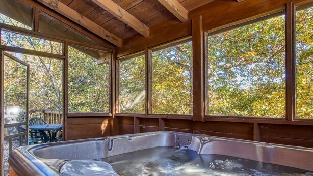 Uma banheira de hidromassagem em uma cabana de madeira com grandes janelas e vista para árvores de outono.