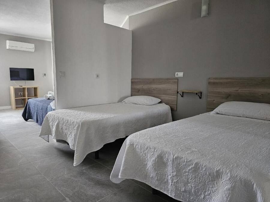 Quarto de hotel com duas camas, televisão e um pequeno armário de madeira.