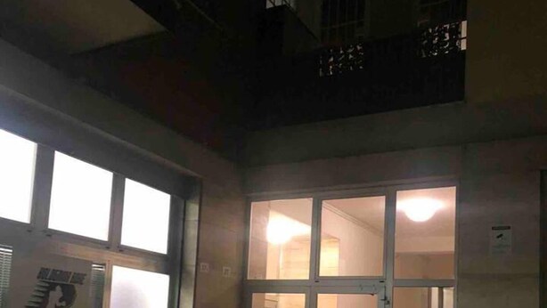 Entrada de um edifício com portas de vidro, corredor interior visível e uma seta amarela apontando para a direita.