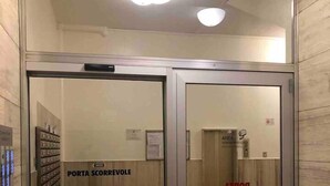 Entrada de hotel com porta giratória, balcão de segurança e sinal de área restrita.