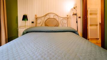 Cama bem arrumada com cabeceira acolchoada, luminária de cabeceira e termostato na parede.