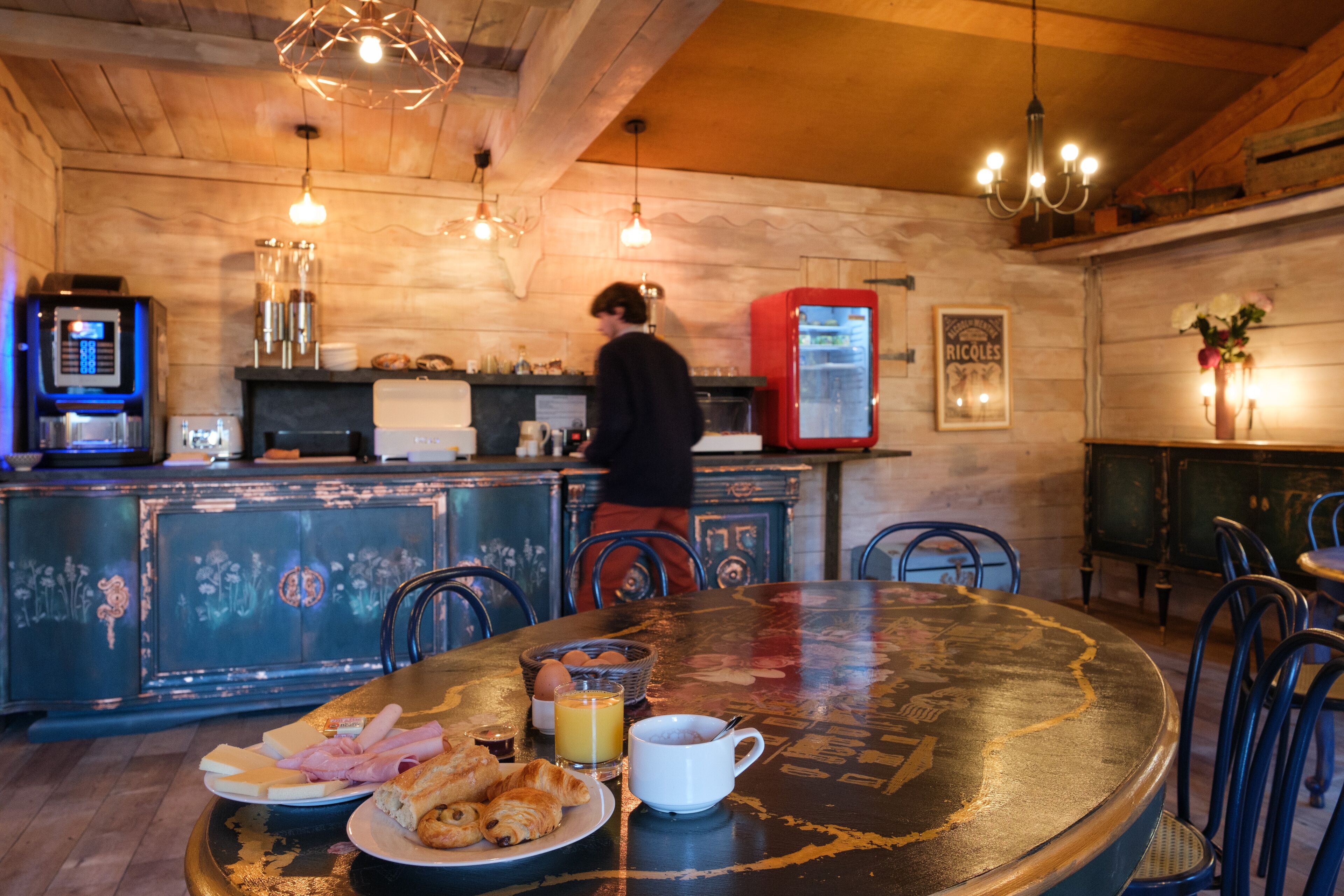 Uma zona de refeições rústica com uma mesa de madeira, cadeiras e uma apresentação de café da manhã com croissants, ovos e suco.