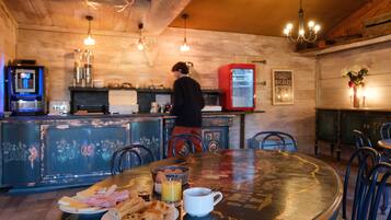 Uma zona de refeições rústica com uma mesa de madeira, cadeiras e uma apresentação de café da manhã com croissants, ovos e suco.