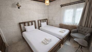 Quarto com duas camas de solteiro, uma cadeira de madeira, um radiador e uma janela com cortinas.