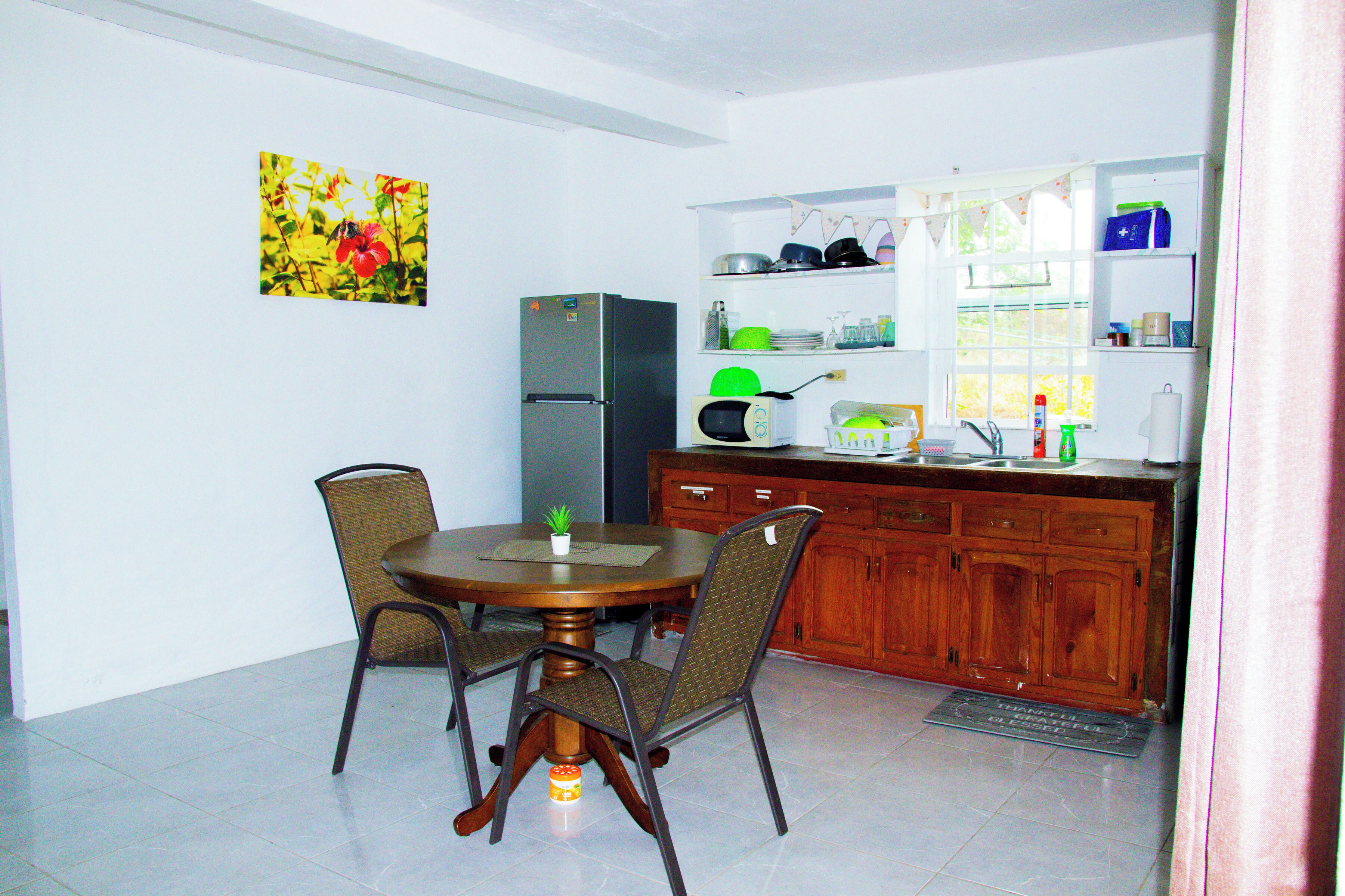 Uma sala de jantar com uma mesa redonda, cadeiras, geladeira, micro-ondas e uma janela com vista.