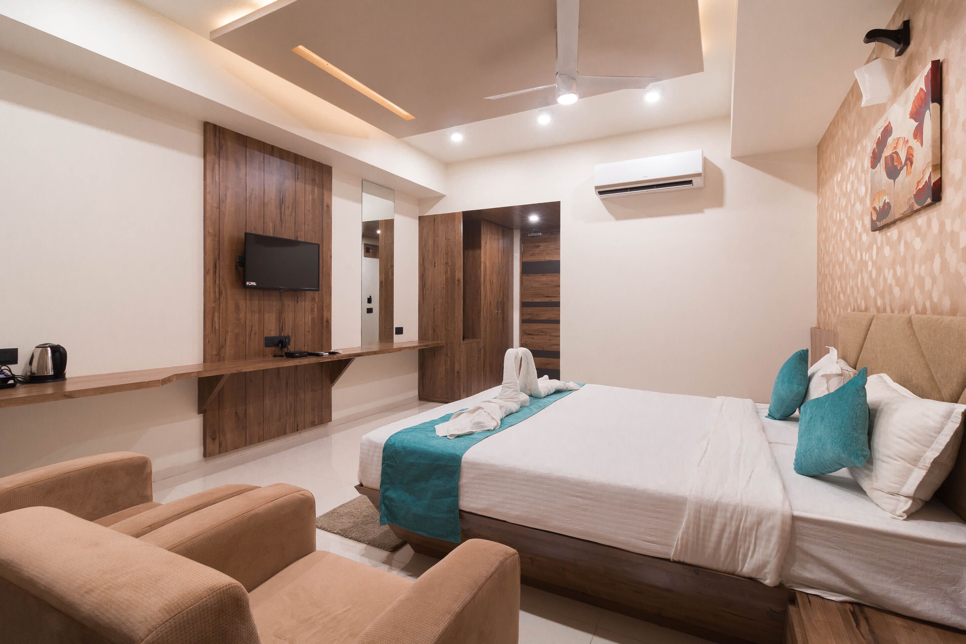 Quarto de hotel moderno com uma cama grande, televisão de tela plana, painel de parede em madeira e uma pequena área de estar.