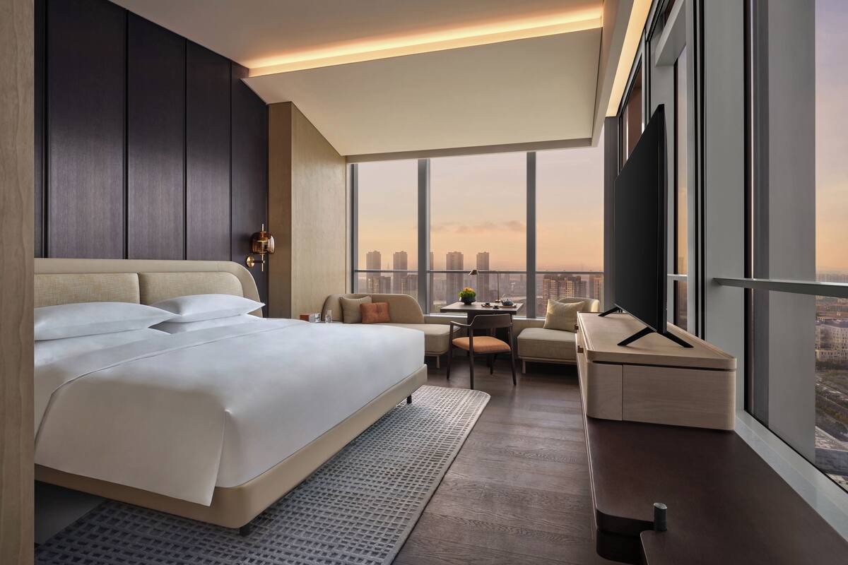 Quarto de hotel moderno com uma cama grande, uma escrivaninha e vista para a cidade.