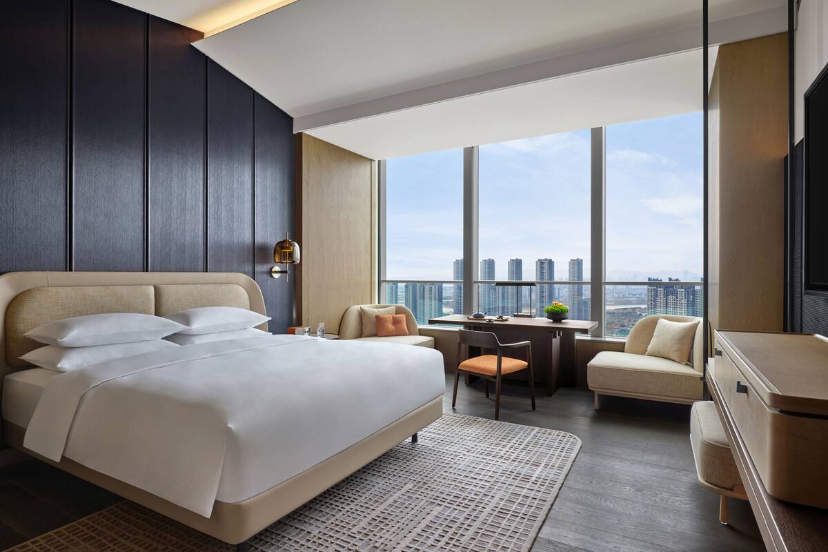 Quarto de hotel moderno com uma cama grande, uma escrivaninha e vista para a paisagem urbana.
