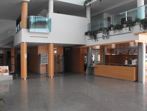Um hall amplo com um balcão de recepção, uma escada e um guarda-corpo de vidro com vista para o nível inferior.