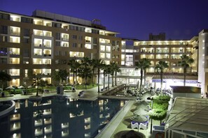 Um hotel com vários andares, piscina ao ar livre, palmeiras e varandas bem iluminadas.
