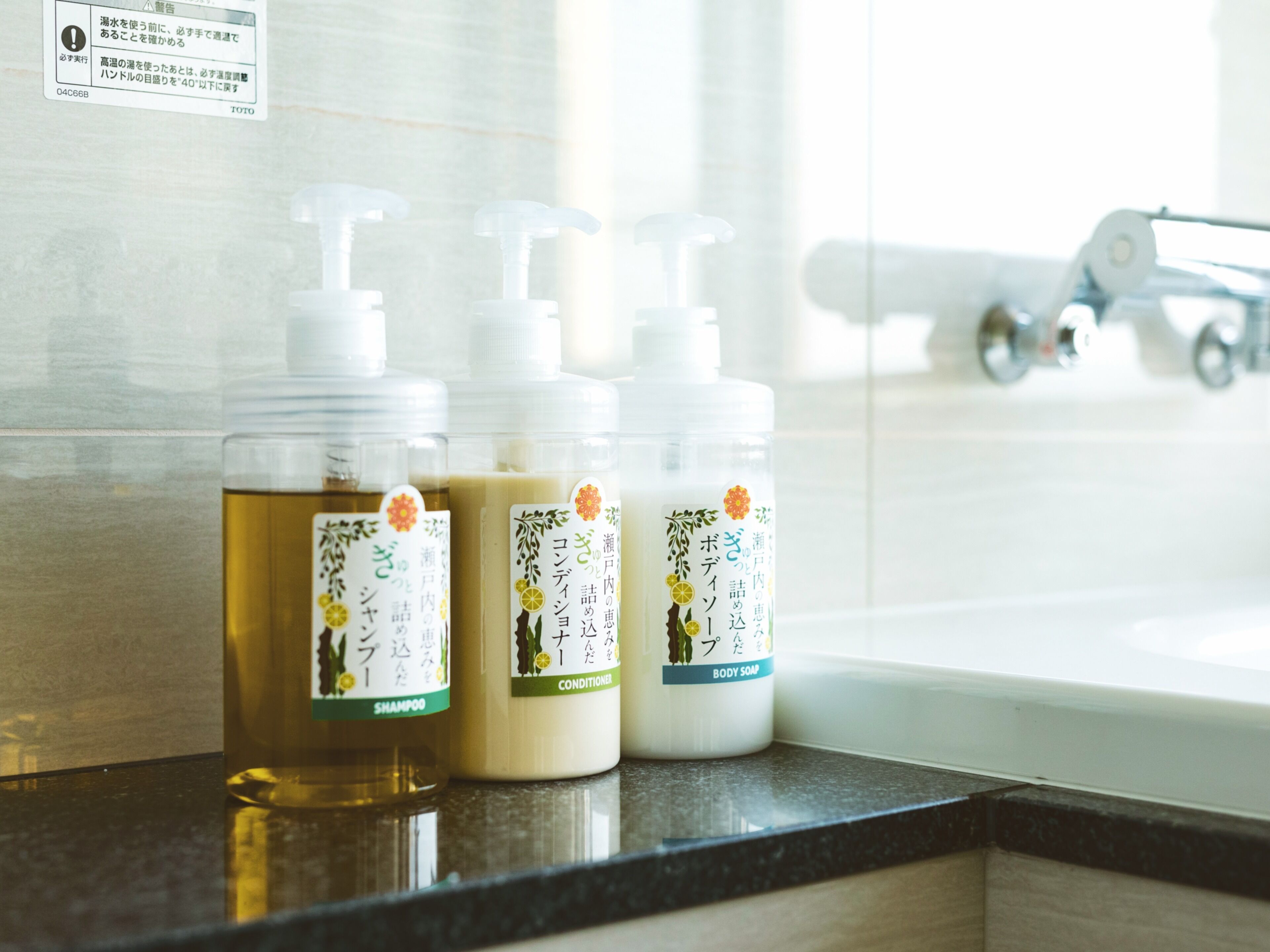 Uma bancada de banheiro com três frascos de shampoo e condicionador, e um dosador de sabonete líquido.