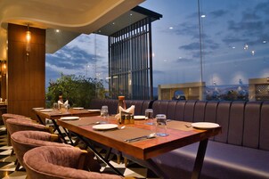 Restaurante com mesa comprida posta para refeição, assentos acolchoados e vista para o céu.