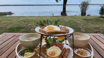 Arrumação de piquenique com comida e bebidas sobre uma mesa de madeira à beira de um lago.