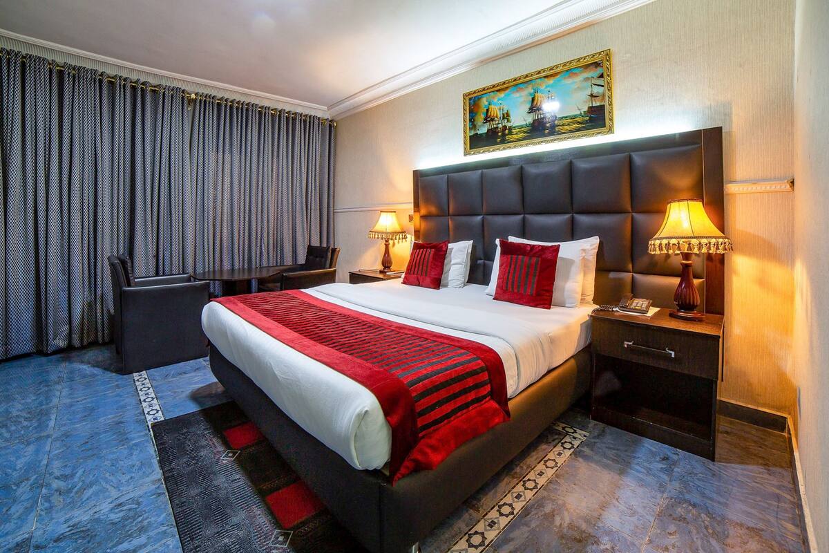 Quarto de hotel com uma cama grande, duas mesas de cabeceira, uma escrivaninha e uma cadeira.