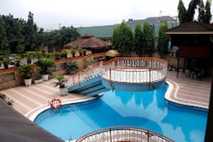 Piscina com cerca vermelha e branca, rodeada por plantas em vasos e um gazebo.