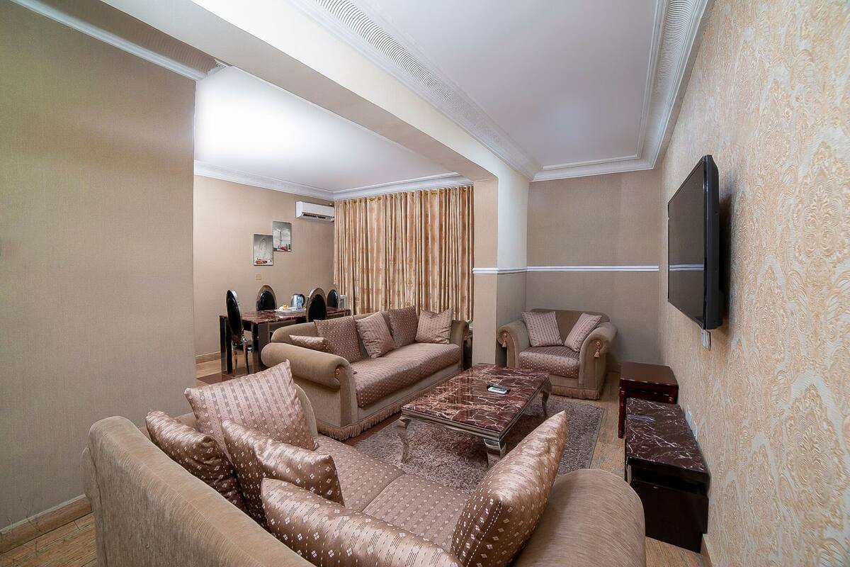 Uma sala de estar com sofá, mesa de centro e televisão na parede.