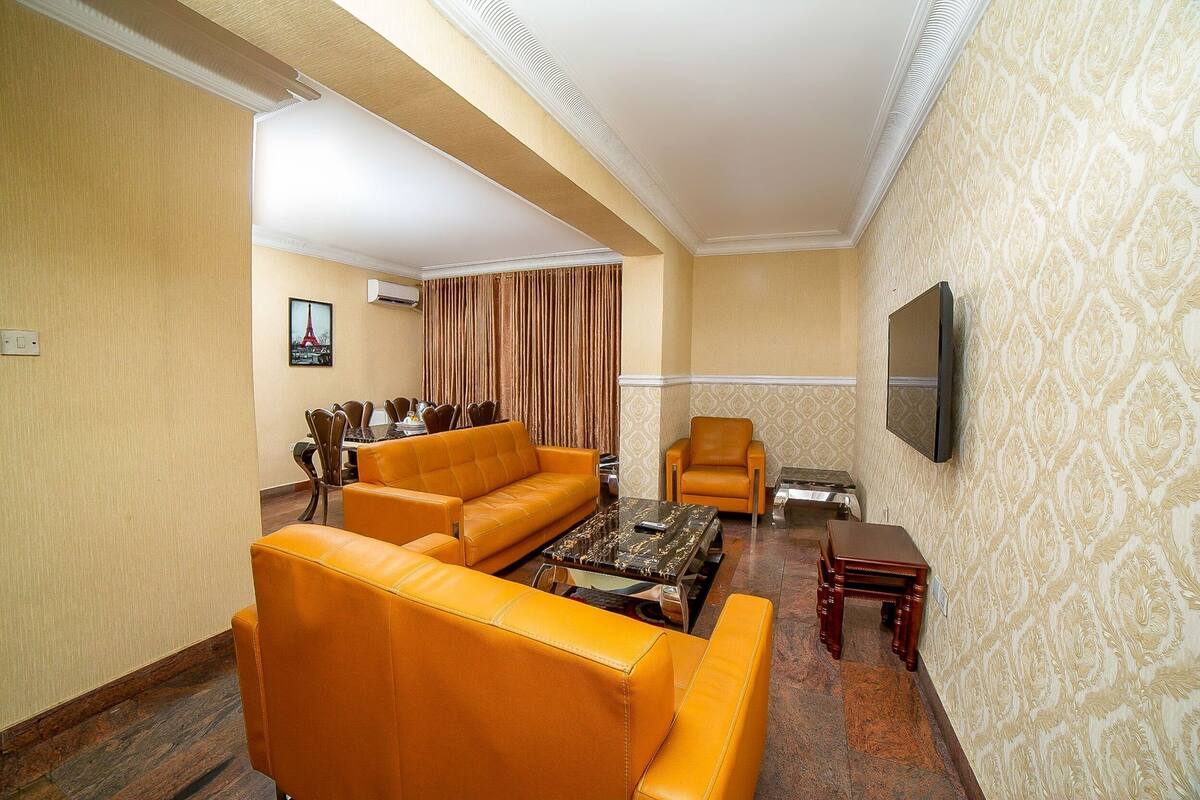 Quarto de hotel com área de estar, incluindo sofá, mesa de centro e televisão fixada na parede.