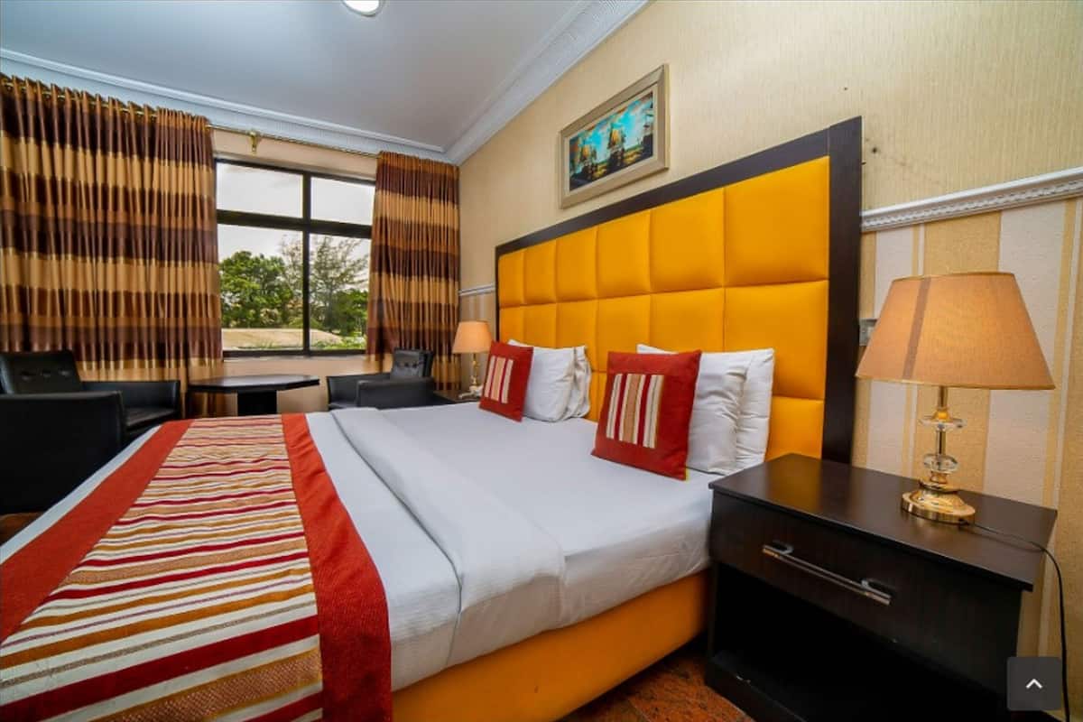 Quarto de hotel com uma cama grande, uma escrivaninha, uma cadeira e uma janela com cortinas.