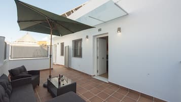 Um terraço no telhado com um grande guarda-sol, móveis de vime e uma mesa de vidro.