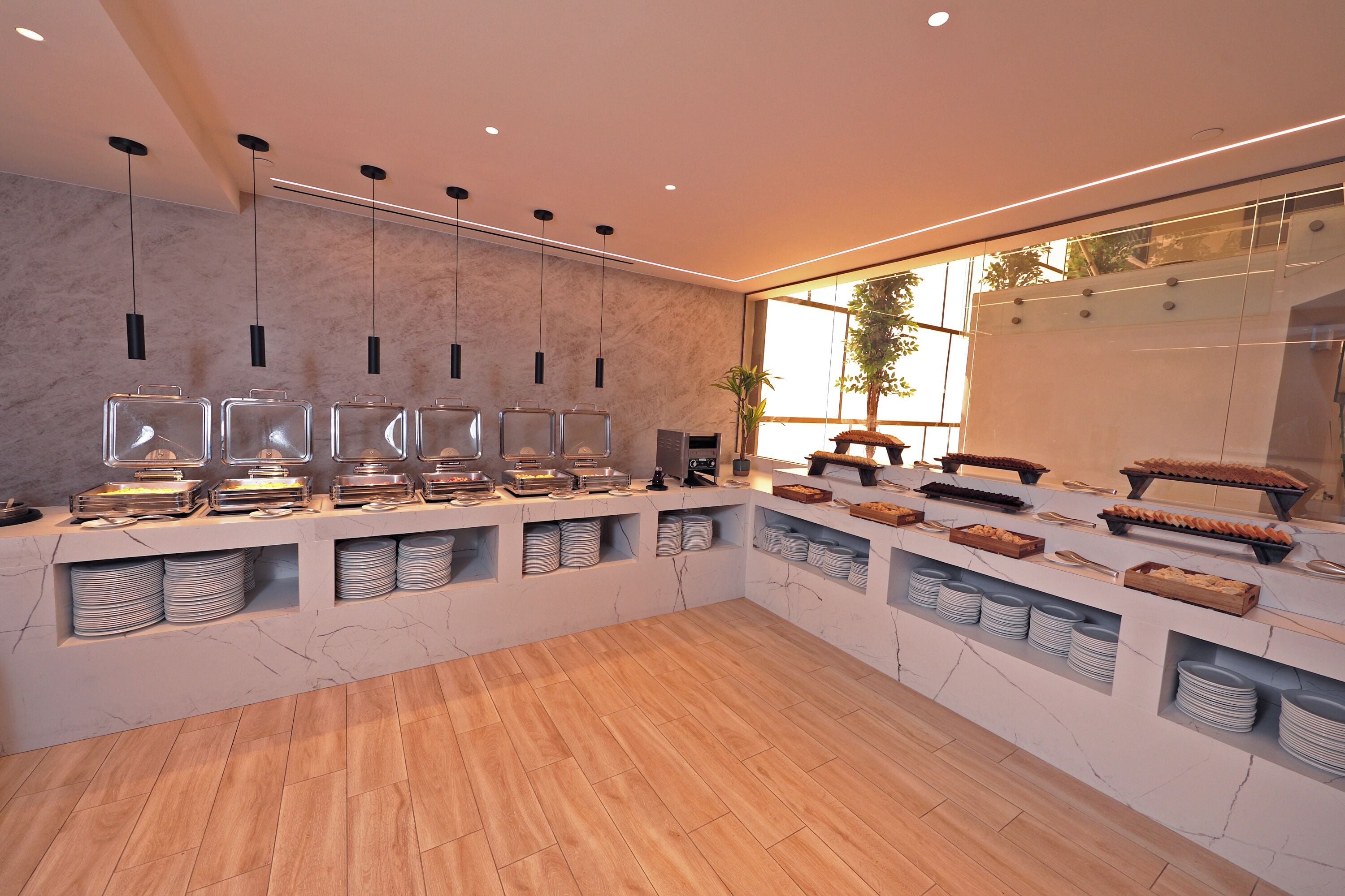 Disposição moderna de buffet com diversas estações de serviço, bancada de mármore e piso de madeira.